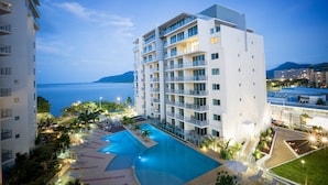 Um hotel moderno com várias varandas, uma piscina e vista para o mar.
