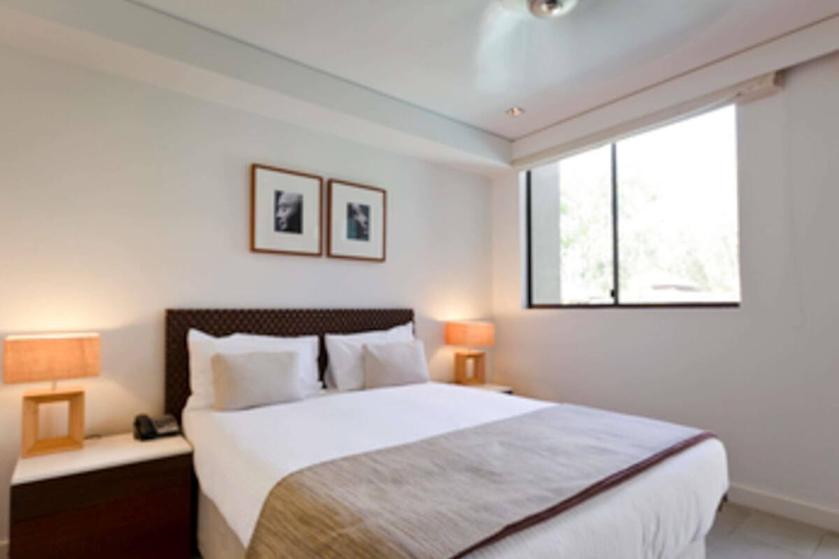 Um quarto bem organizado com uma cama grande, duas mesas de cabeceira com abajures e duas molduras na parede.