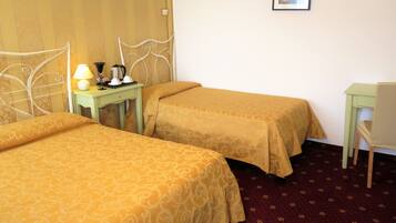 Quarto de hotel com duas camas de solteiro, uma pequena mesa com abajur, uma cadeira e um quadro pendurado na parede.