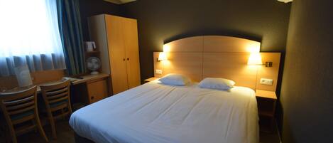 Quarto de hotel com uma cama grande, uma escrivaninha com cadeira, um guarda-roupa e luminárias de cabeceira.