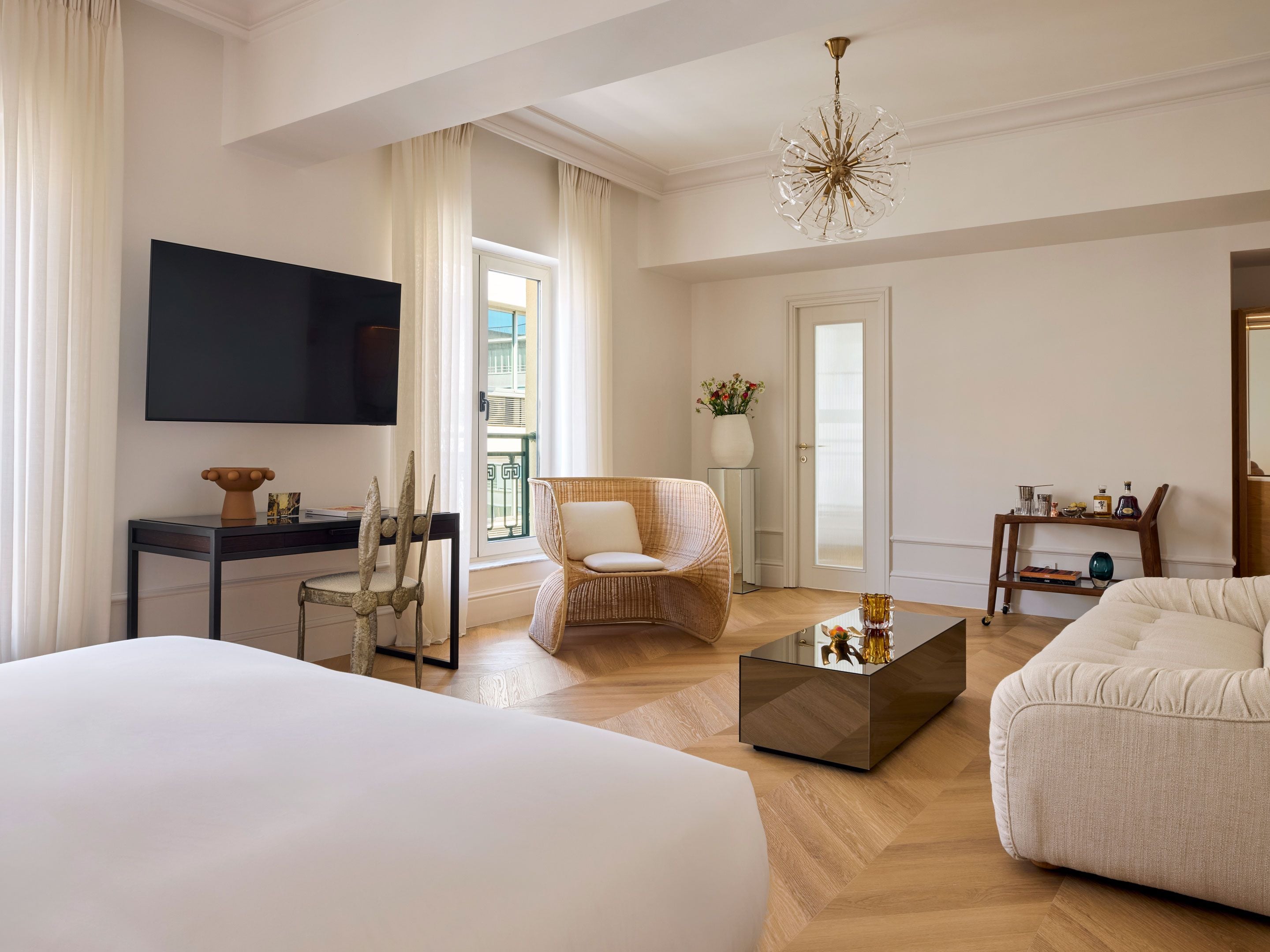 Quarto de hotel moderno com uma cama grande, uma escrivaninha, uma cadeira, uma mesa de centro e televisão fixada na parede.