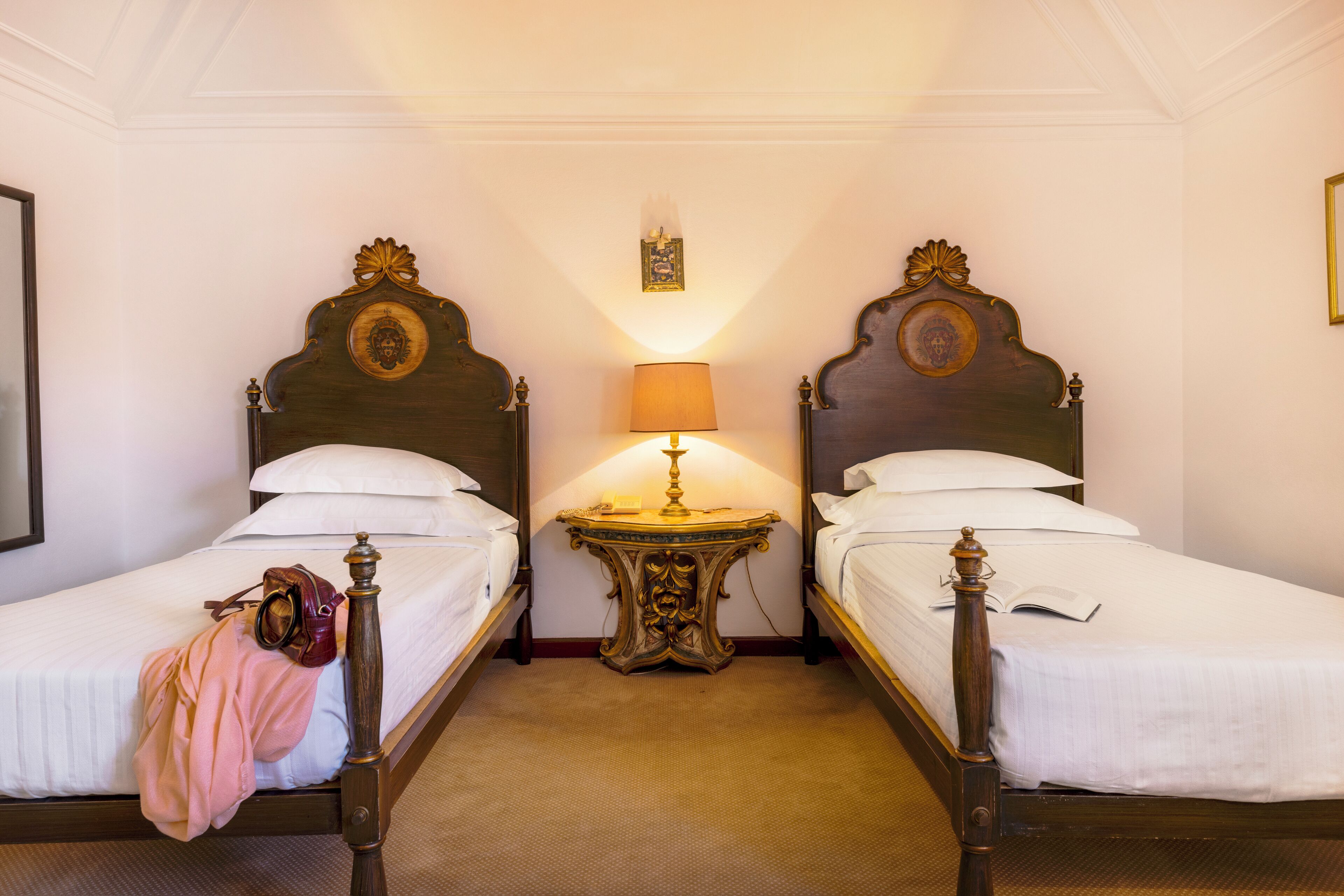 Quarto de hotel com duas camas de madeira, uma mesinha com luminária e um quadro na parede.