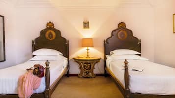 Quarto de hotel com duas camas de madeira, uma mesinha com luminária e um quadro na parede.