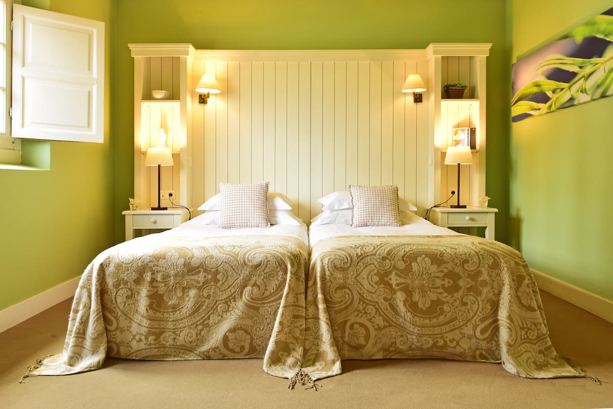 Uma cama de casal com cabeceiras iguais, abajures nas laterais e uma parede verde.