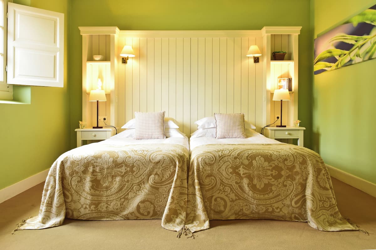 Quarto com duas camas, cada uma com colcha estampada, abajures e uma prateleira fixada na parede com uma planta.