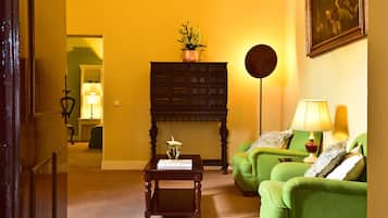 Quarto com sofá verde, mesinha de madeira escura com um livro, uma pequena planta em vaso e um espelho redondo fixado na parede.