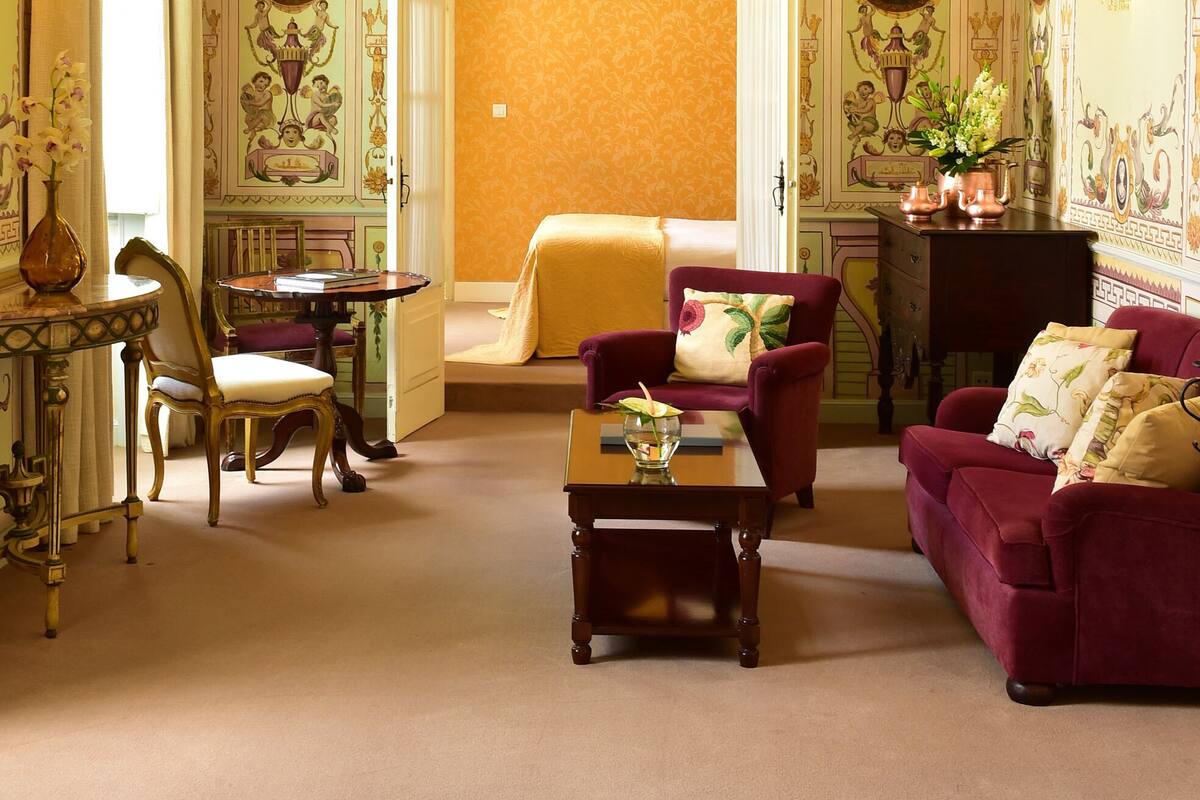 Um quarto luxuoso com arte decorativa no teto, um candelabro e móveis clássicos.