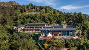 Um hotel grande, com vários andares, e fachada em azul e castanho, localizado numa encosta rodeada por vegetação exuberante.