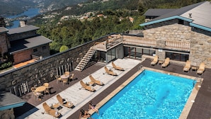 Piscina no terraço com espreguiçadeiras e vista para um lago e montanhas.