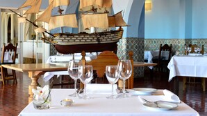Mesa de jantar posta com toalha branca, copos de vinho e um modelo de navio.