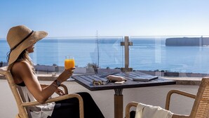 Alguém sentado à mesa com um copo de suco de laranja, com vista para o litoral.