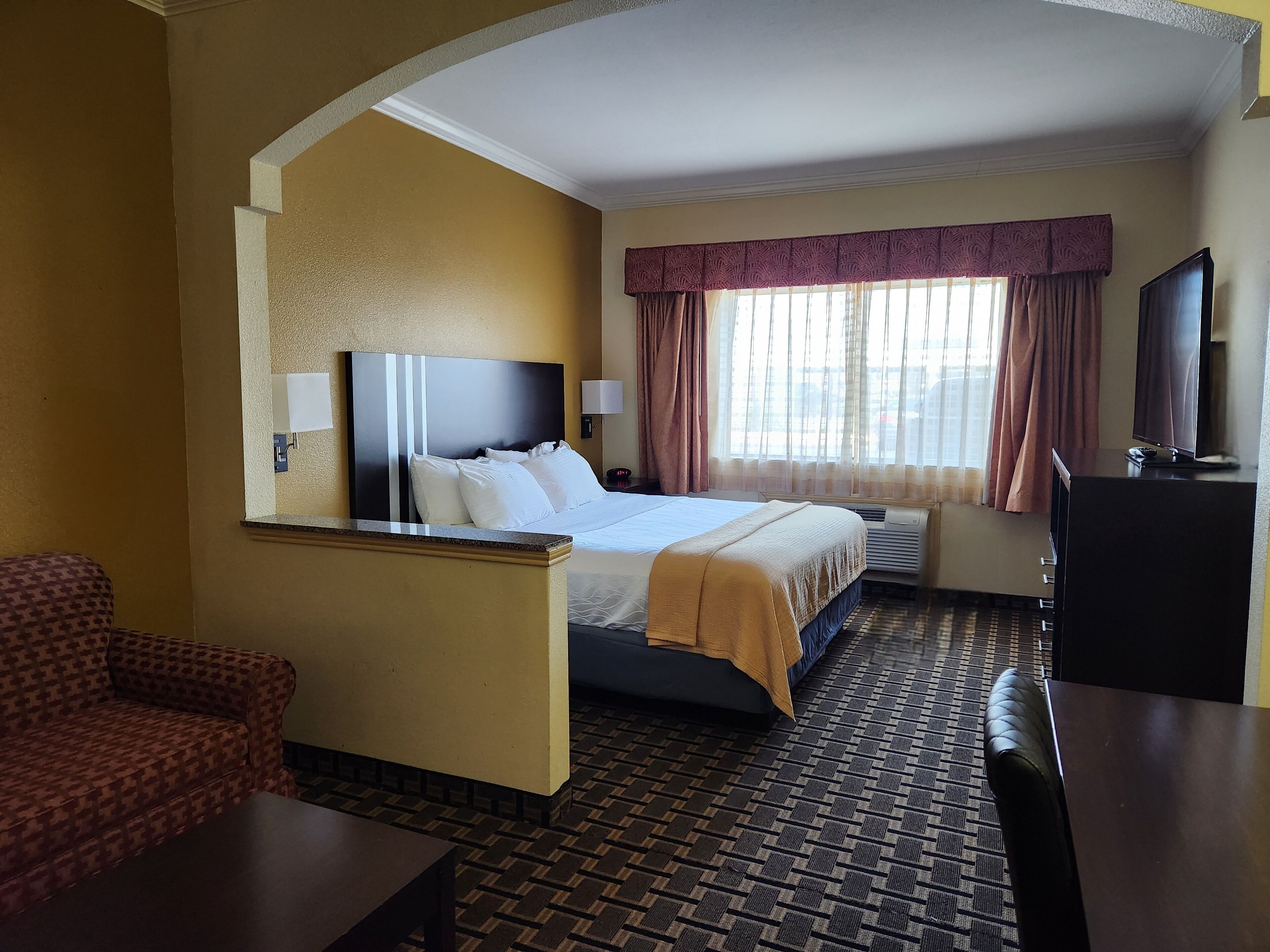 Quarto de hotel com cama, televisão, escrivaninha e cadeira.