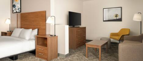 Quarto de hotel com cama, televisão, escrivaninha, cadeira e sofá.