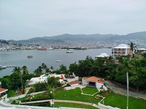 Paisagem costeira com um porto de iates, edifícios residenciais e vegetação exuberante.