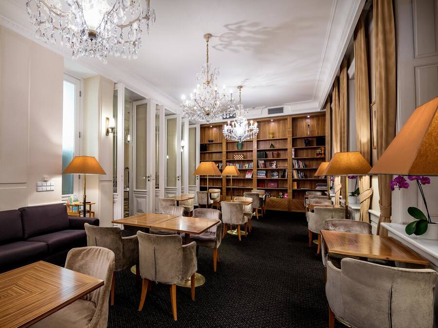 Uma biblioteca ampla com tetos altos, lustres ornamentados e diversas opções de assentos, incluindo mesas e cadeiras.