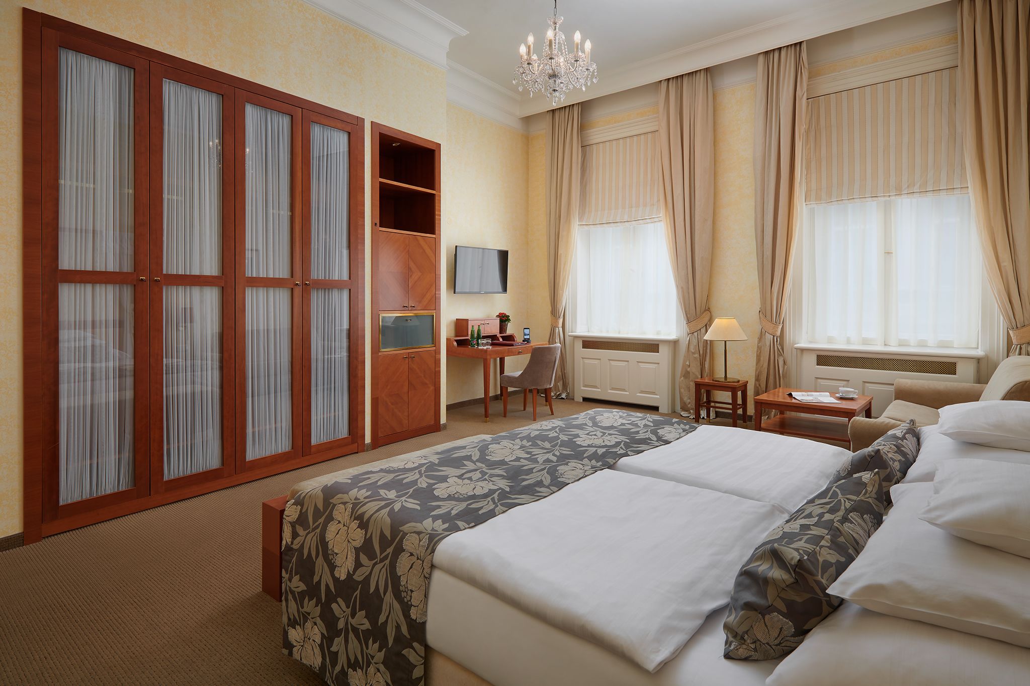 Quarto de hotel com uma cama grande, uma escrivaninha com cadeira, uma televisão e um guarda-roupa com portas de correr.