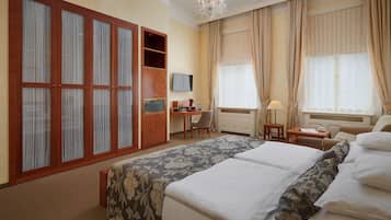 Quarto de hotel com uma cama grande, uma escrivaninha com cadeira, uma televisão e um guarda-roupa com portas de correr.