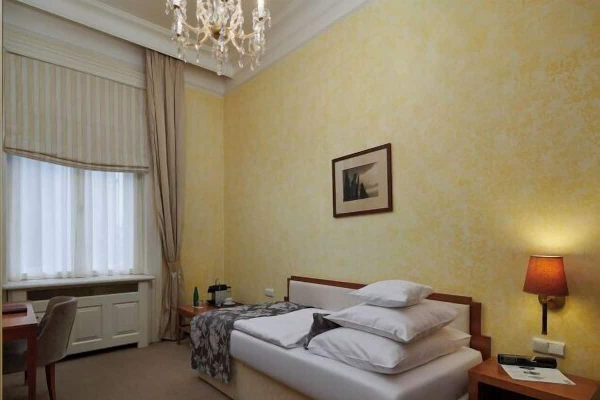 Quarto de hotel com cama, escrivaninha, cadeira, abajur e um quadro na parede.