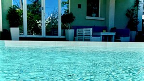 Piscina com água cristalina, cercada por um edifício com janelas amplas e plantas em vasos.