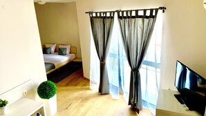 Quarto de hotel com cama, cortinas, televisão e uma pequena planta.