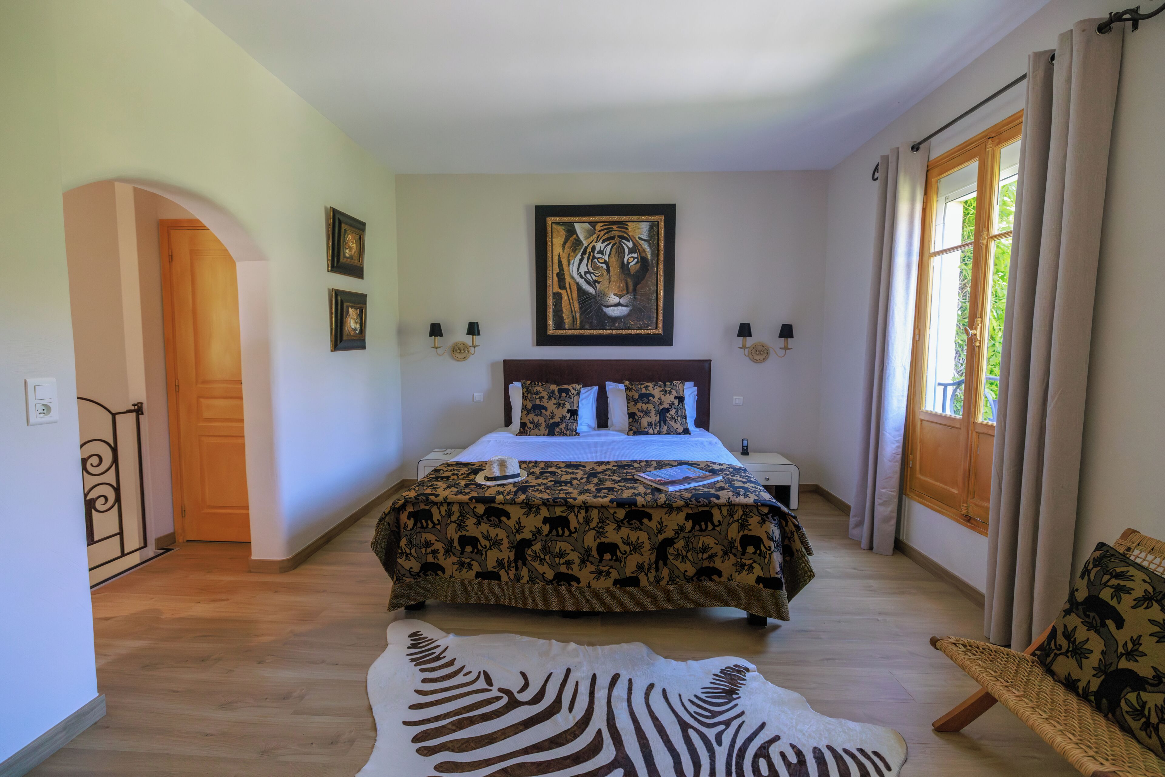 Um quarto com uma cama, um tapete de zebra, um quadro de tigre e uma porta.