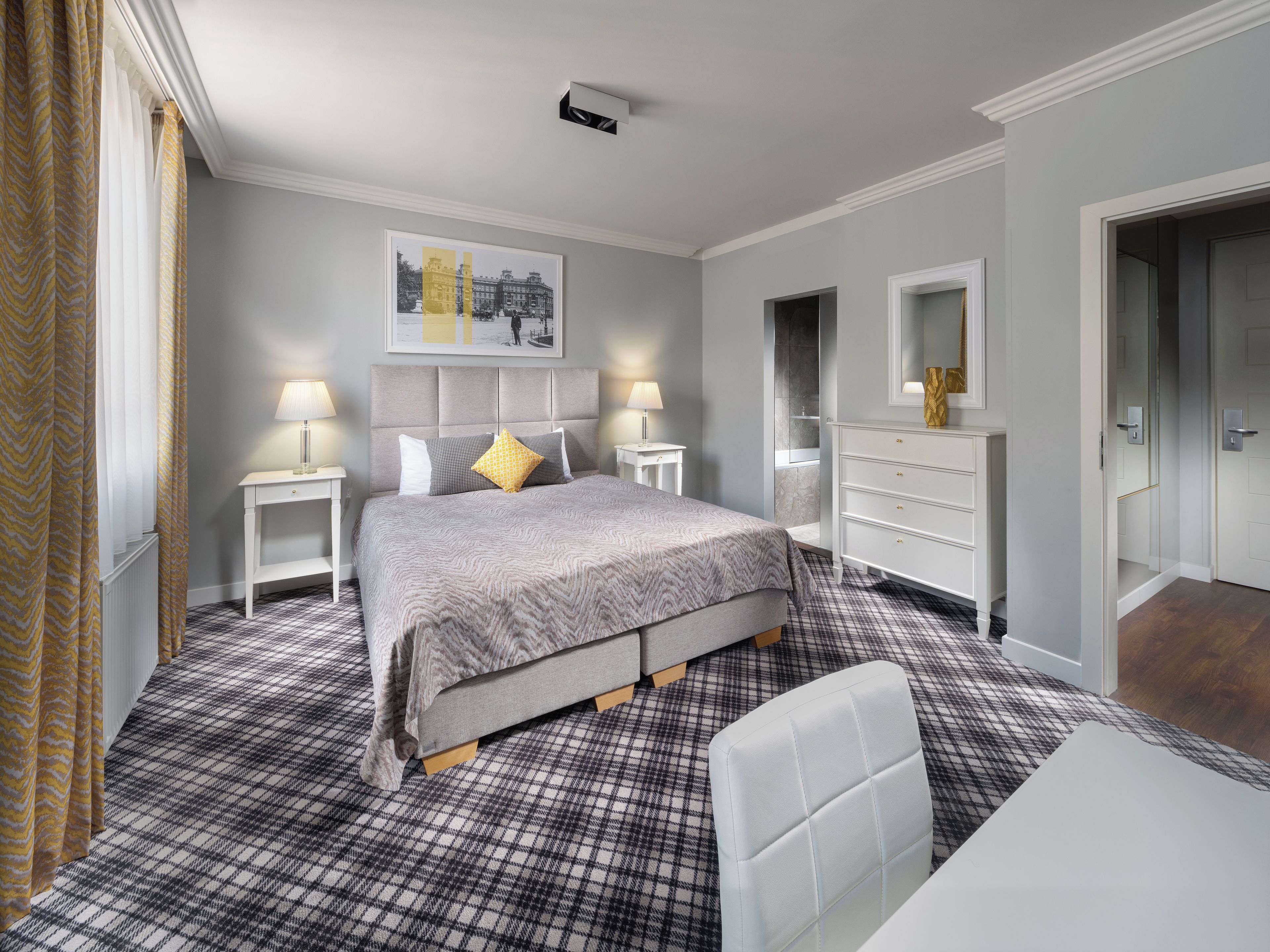 Quarto de hotel com cama, mesas de cabeceira, cômoda, espelho e um quadro na parede.