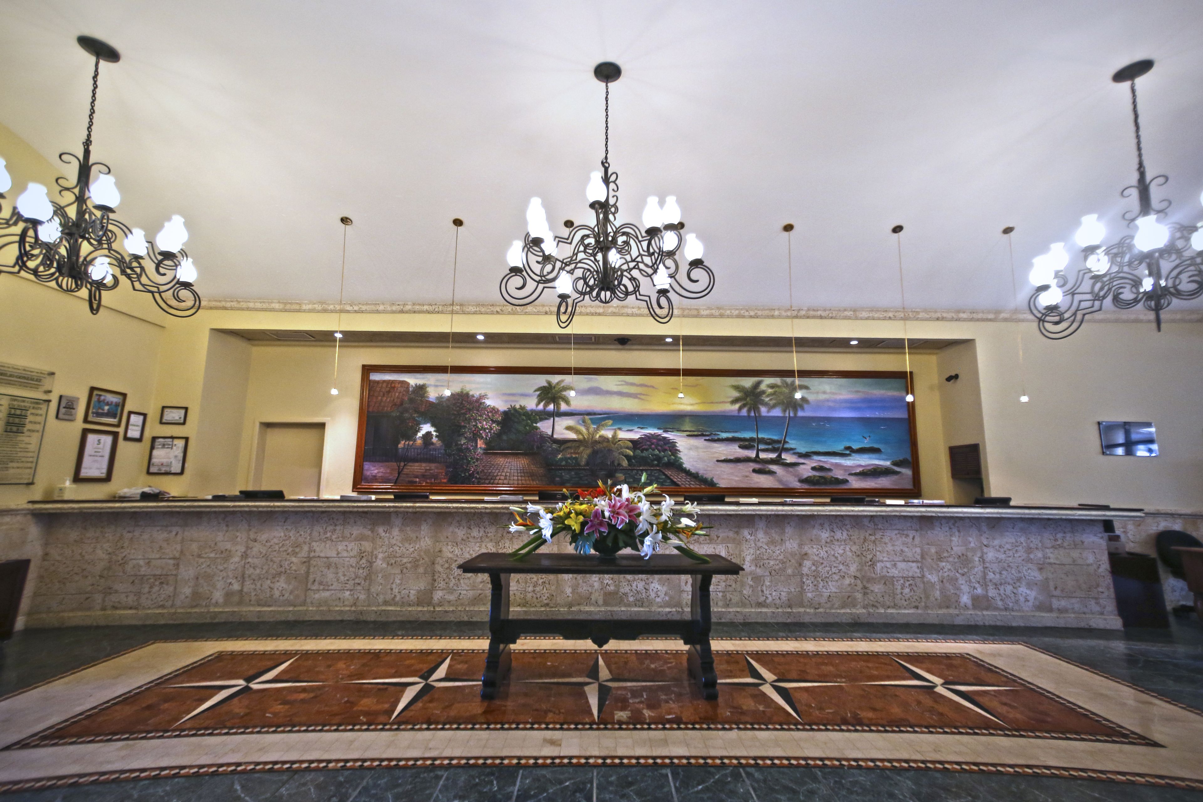 Um hall de entrada com uma receção, um candelabro, uma grande pintura com uma cena de praia e uma composição floral sobre a mesa.