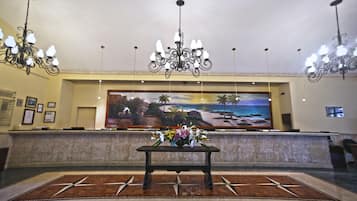 Um hall de entrada com uma receção, um candelabro, uma grande pintura com uma cena de praia e uma composição floral sobre a mesa.