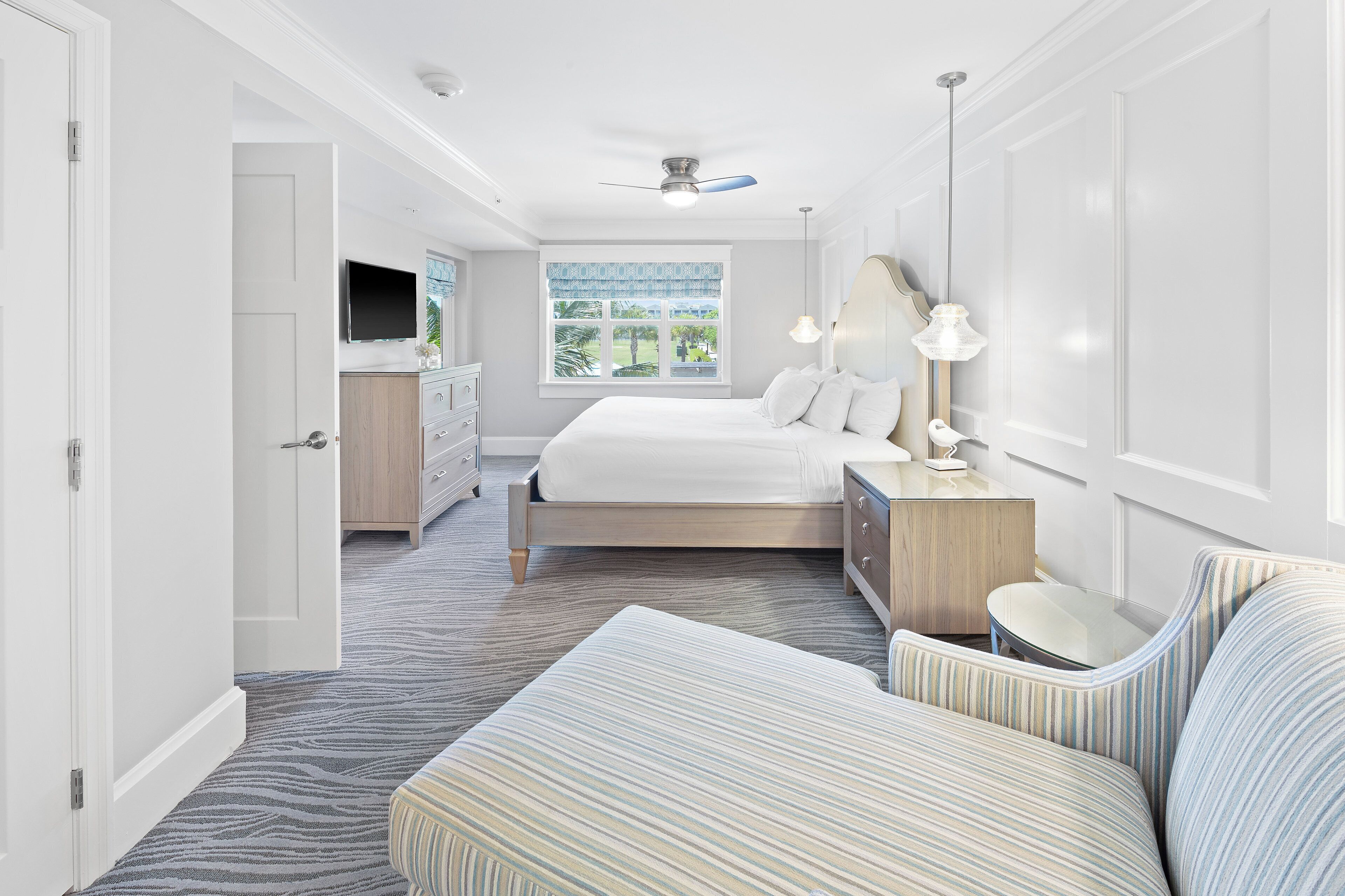 Quarto de hotel com cama, mesa de cabeceira, luminária e vista para o exterior.