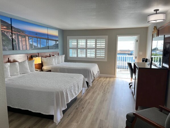Quarto de hotel com duas camas, uma escrivaninha, uma cadeira e uma janela grande com persianas.