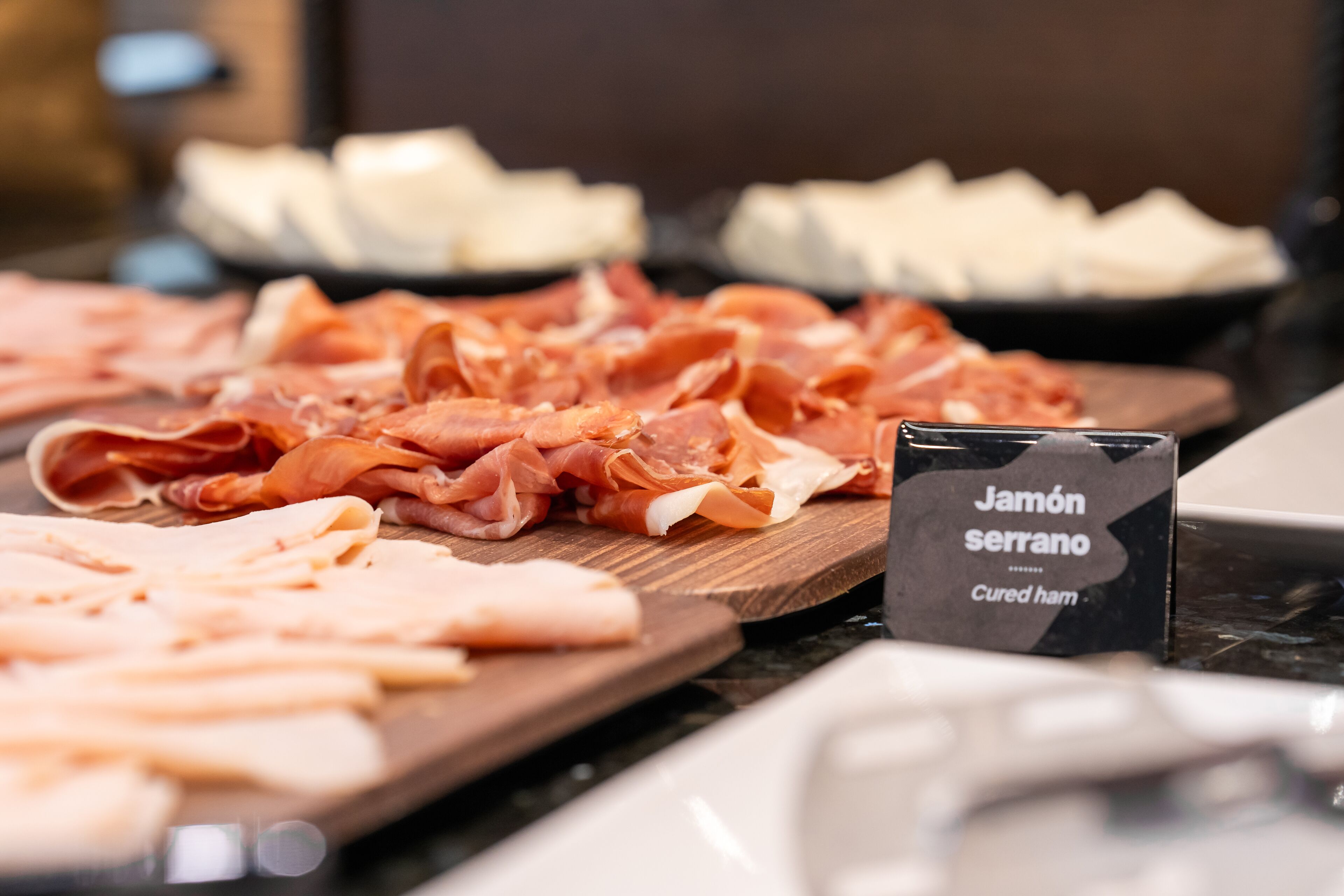Uma seleção de presunto curado em uma tábua de madeira com uma etiqueta que diz "Jamón serrano presunto curado".