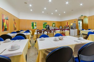 Uma sala de jantar com mesas preparadas para o serviço, cadeiras e um buffet.
