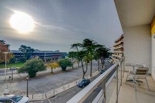 Uma varanda com vista para um estacionamento, árvores e um edifício com bandeiras.