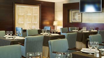 Uma área de refeições de hotel com várias mesas preparadas para o jantar, cada uma com cadeiras e copos de vinho.