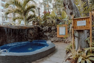 Uma área de spa com hidromassagem, uma placa de madeira com as regras do spa e uma cascata.