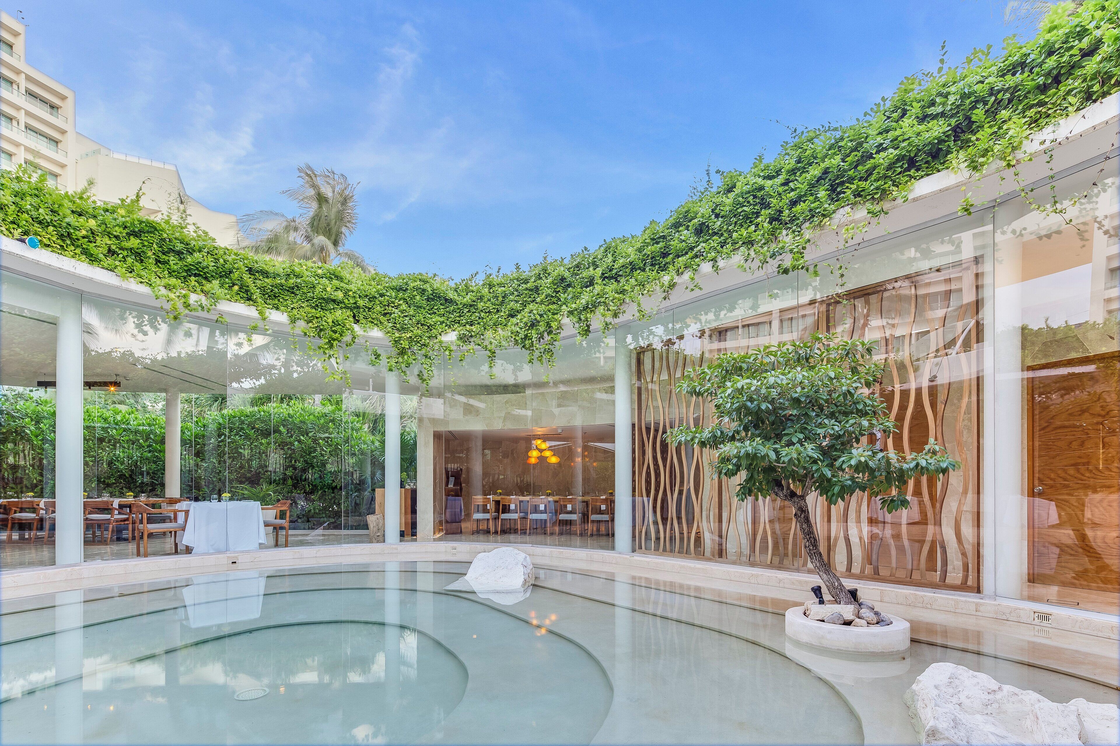 Espaço moderno de piscina interna com estrutura de vidro, área de estar e espaço para refeições visíveis através do vidro.