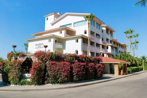 Um hotel de vários andares com fachada branca, varandas e um jardim com flores rosa.