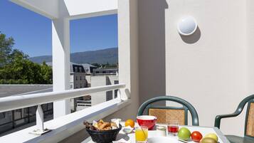 Uma varanda com itens de café da manhã, vista para edifícios e montanhas, e um corrimão branco.