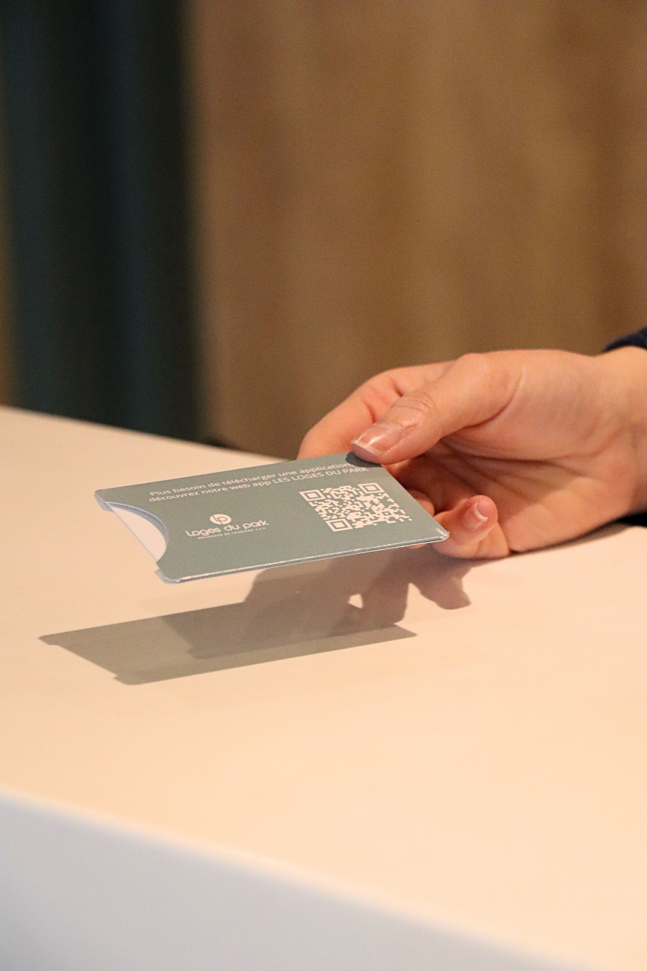 Uma mão segurando um cartão com um código QR e texto, apoiado em uma mesa.
