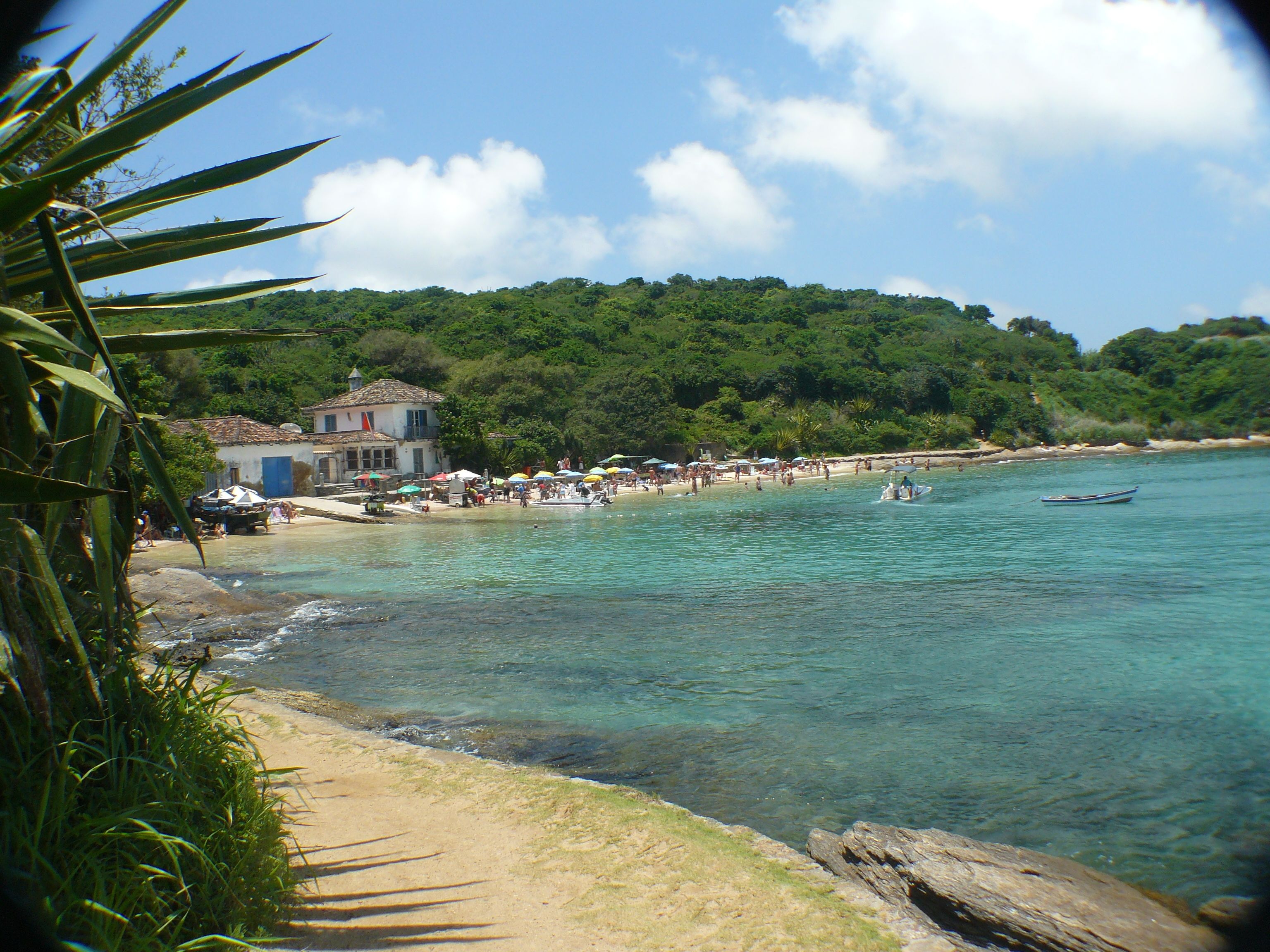 Uma praia com águas turquesa cristalinas, areal arenoso e um edifício com telhado em azulejos.