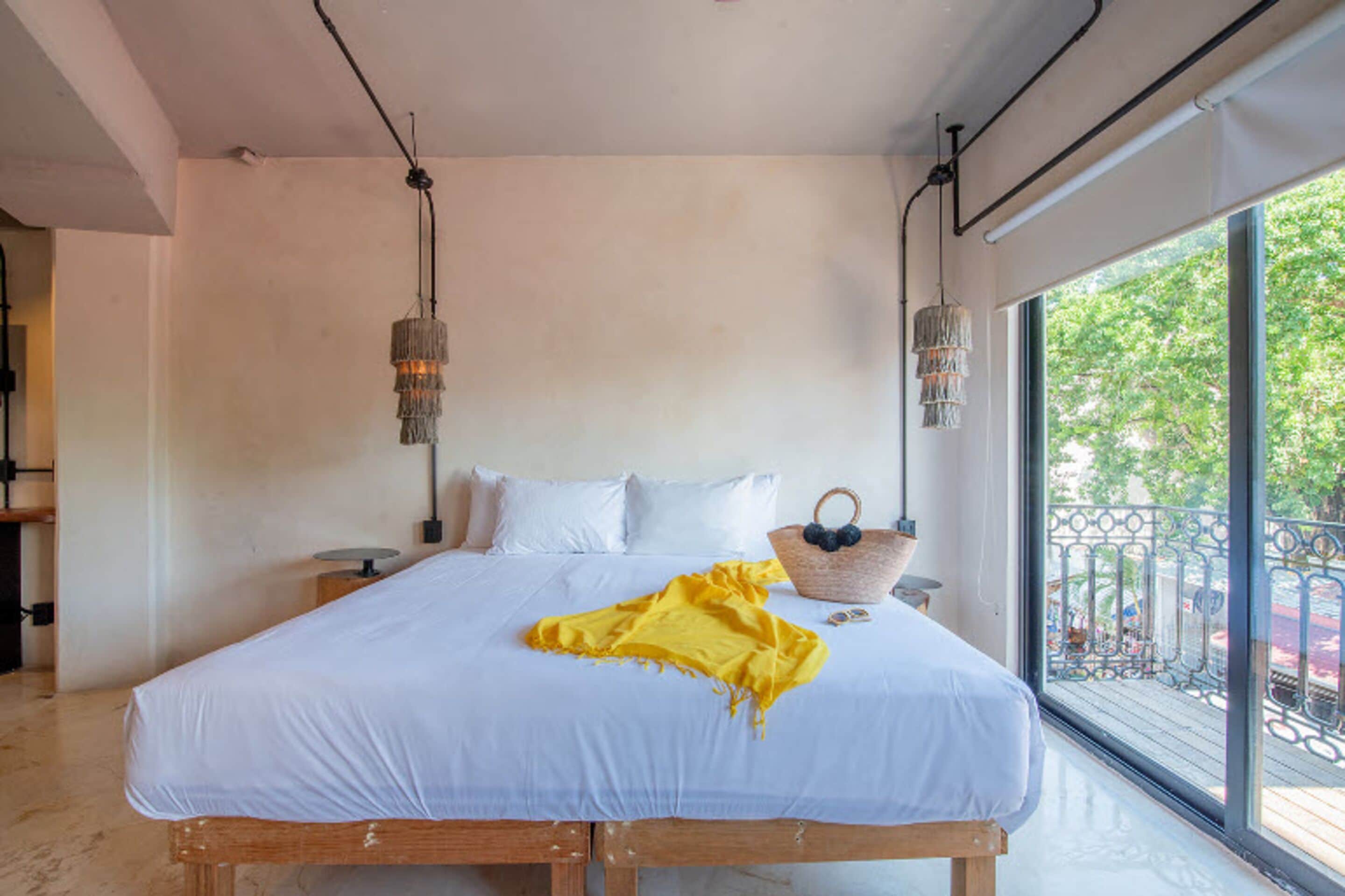 Quarto com uma cama grande, roupa de cama branca, um cobertor amarelo e uma cesta de frutas.