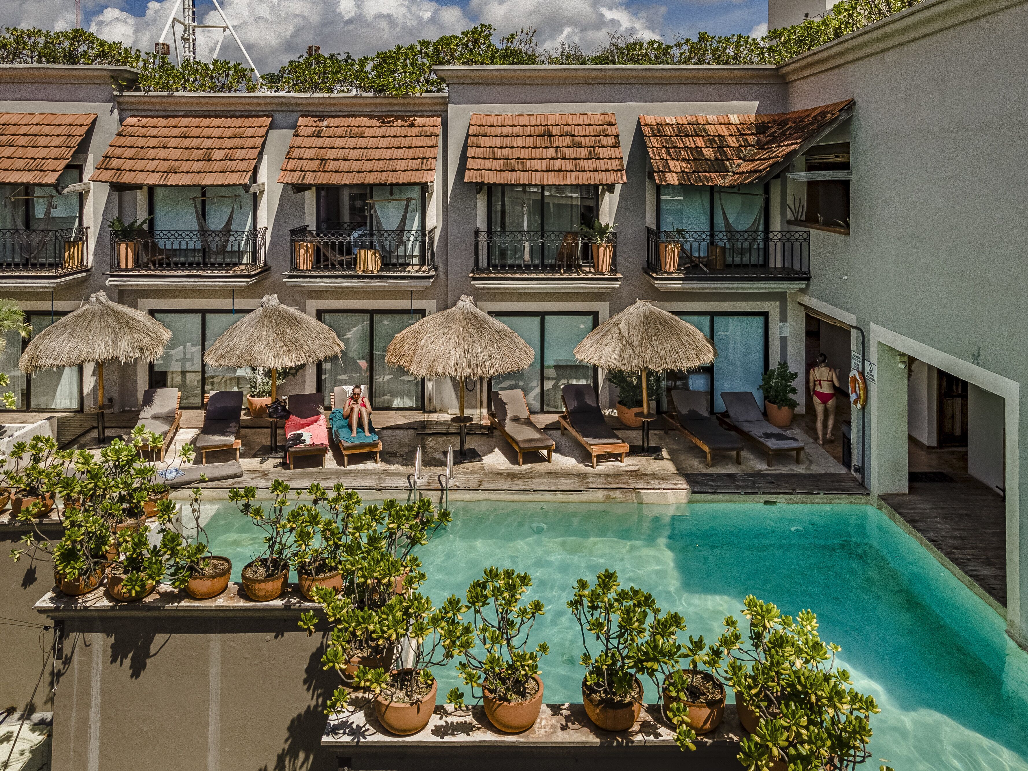 Um hotel com área de piscina, várias espreguiçadeiras e guarda-sóis de palha.