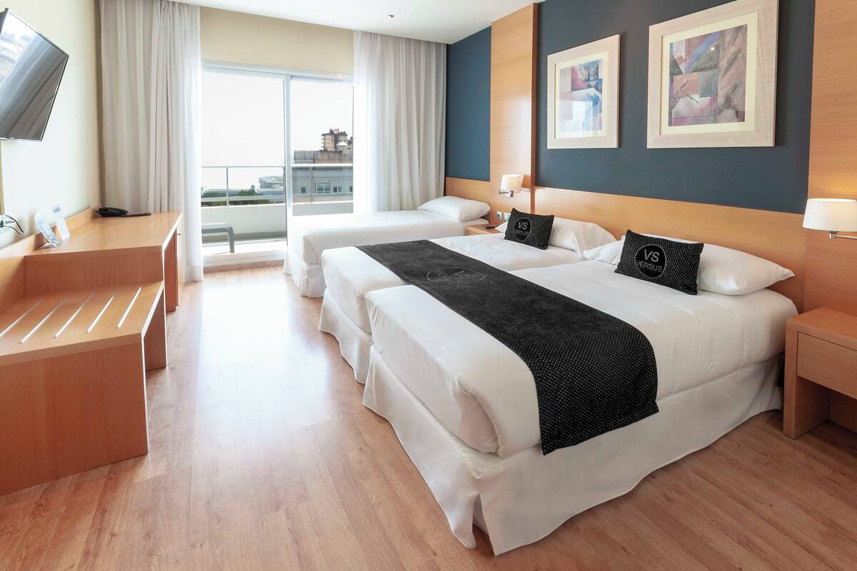 Quarto de hotel com duas camas, uma escrivaninha e vista para a cidade.