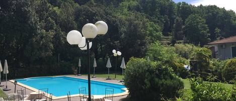 Piscina com um terraço ao redor, incluindo área de estar externa e guarda-sóis.
