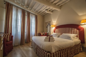 Quarto de hotel com uma cama grande, cortinas listradas, uma cadeira vermelha e um abajur.