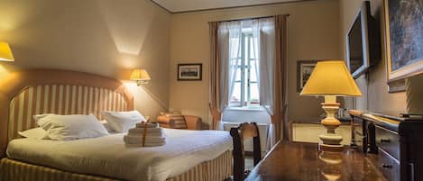 Quarto de hotel com cama, escrivaninha, cadeira, televisão e janela com cortinas.