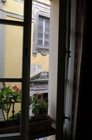 Uma janela com vista para a fachada de um edifício, incluindo outra janela com grades decorativas e uma placa.
