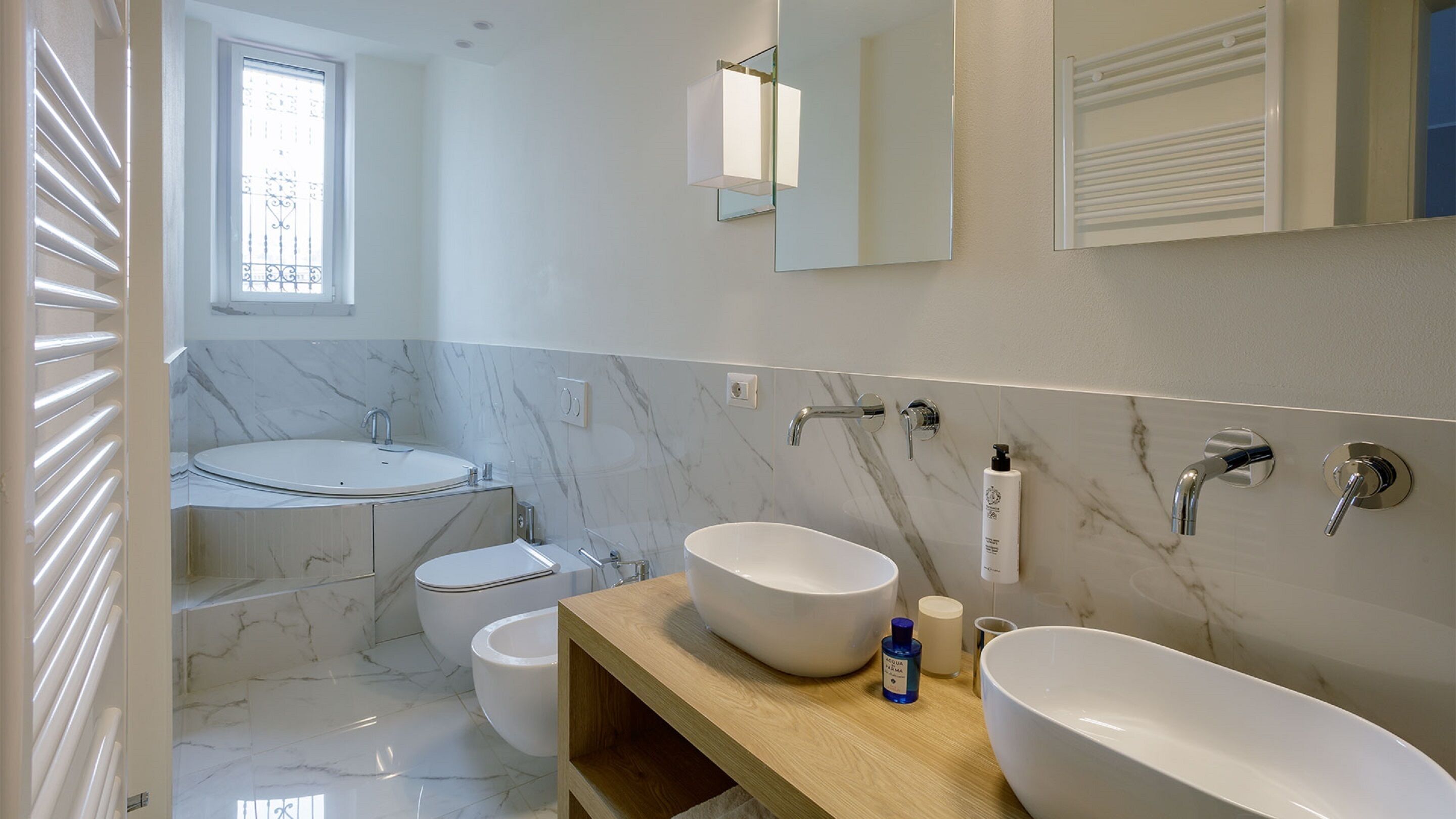 Um banheiro moderno com piso de mármore, uma banheira livre, um lavatório com cuba grande, vaso sanitário e uma janela que proporciona luz natural.