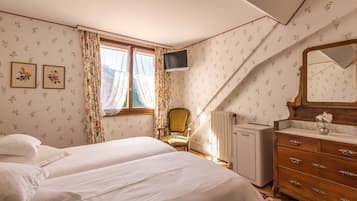 Quarto com duas camas, cómoda de madeira, uma cadeira, radiador, televisão e papel de parede floral.