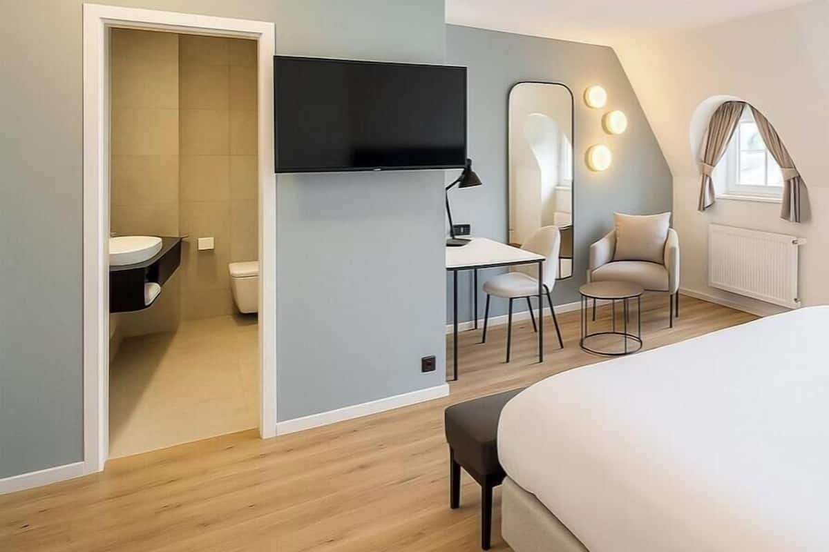 Quarto moderno com cama, escrivaninha, cadeira, televisão e banheiro.
